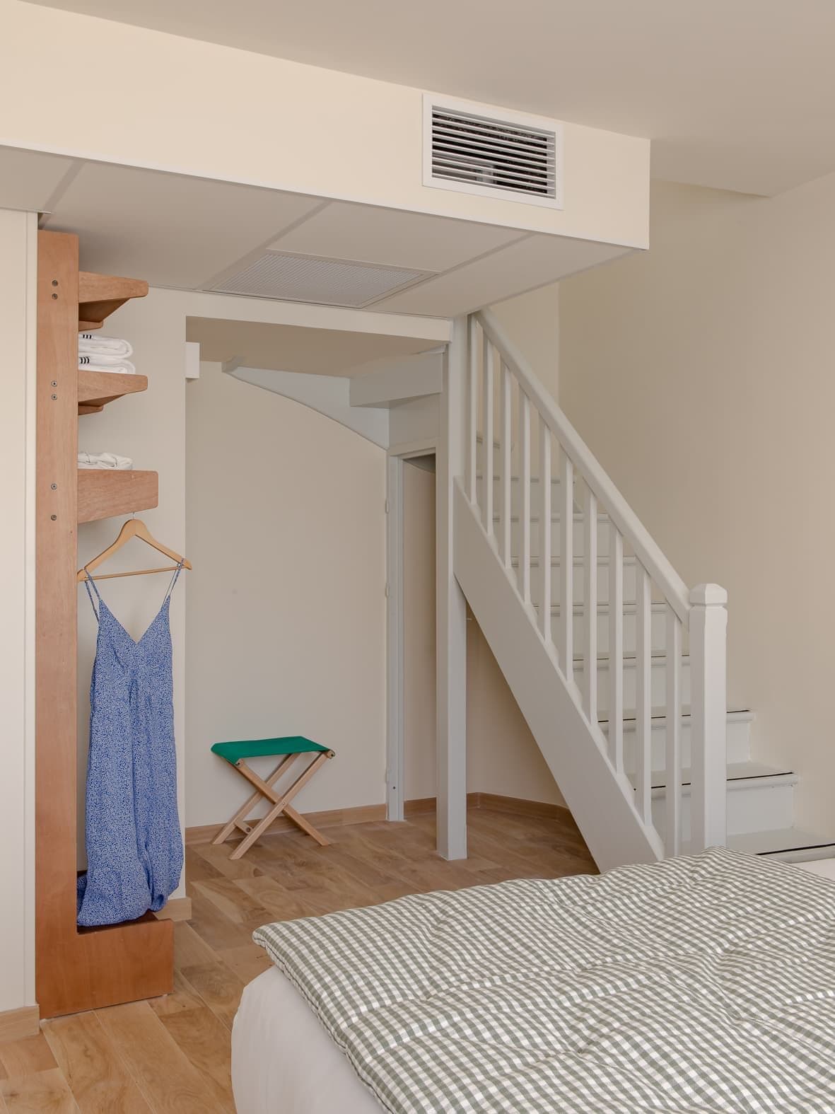 Quarto com uma cama, guarda-roupa de madeira, cabideiro, cadeira dobrável verde e uma escada.