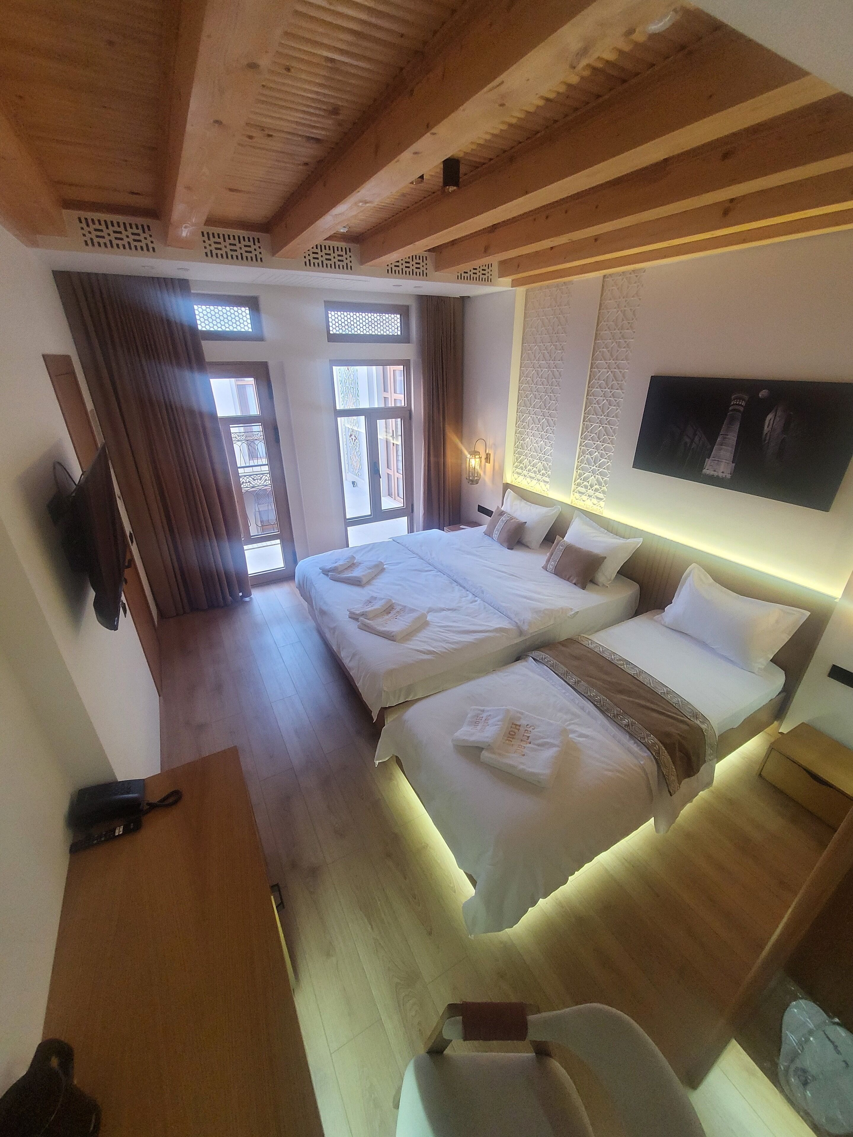 Quarto de hotel com duas camas, uma mesa, uma televisão e uma janela grande.