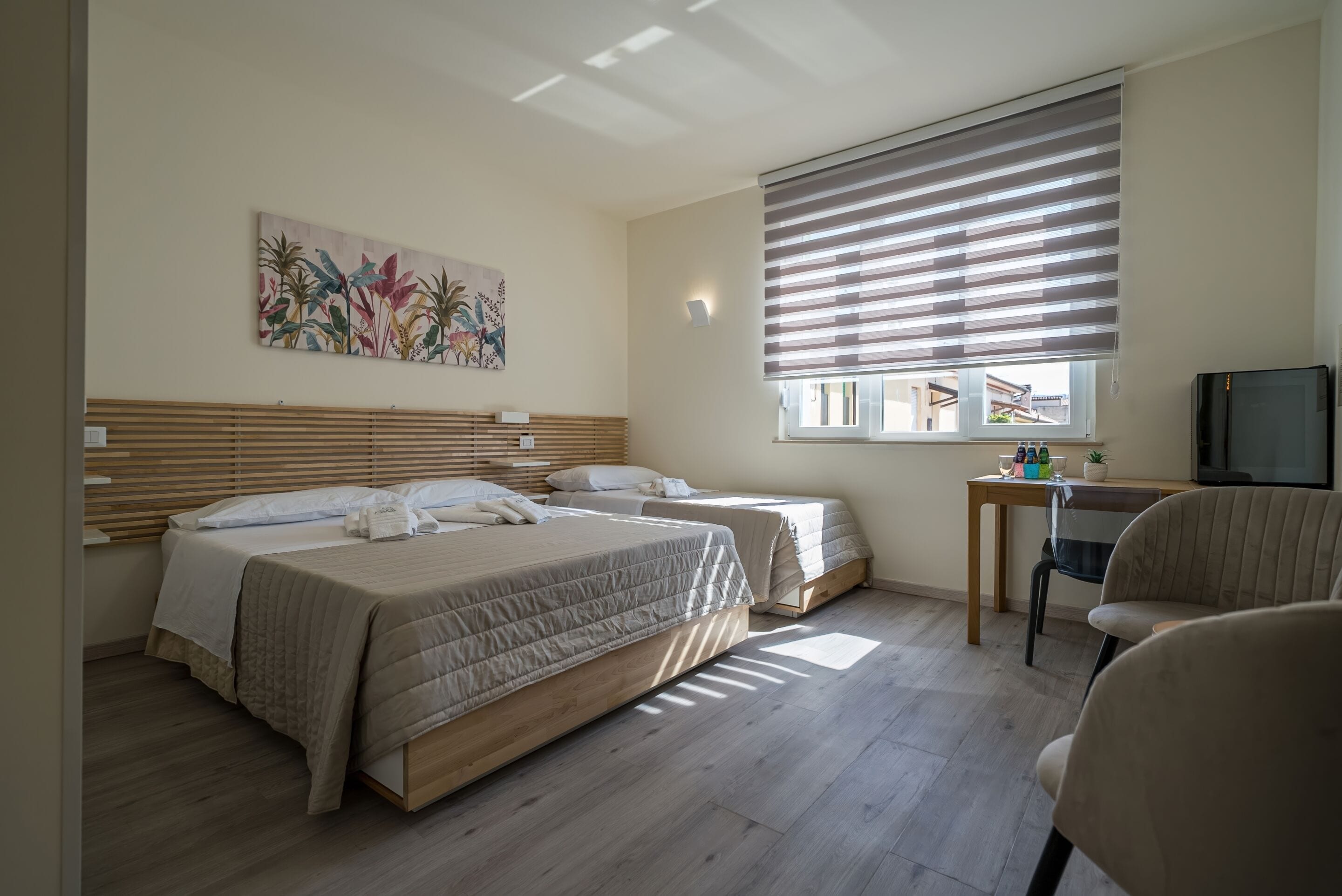 Quarto de hotel com duas camas, televisão, secretária e cadeira, e janela com persianas.