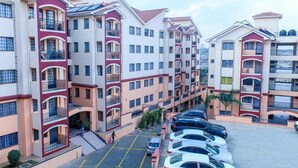 Um edifício residencial com vários andares, varandas, estacionamento e céu claro.