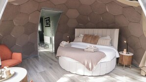 Quarto moderno com uma cama redonda, uma cadeira vermelha e uma pequena mesa redonda com objetos decorativos.