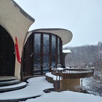Um edifício com uma grande porta de vidro e janelas, uma bandeira à esquerda e um alpendre coberto de neve.
