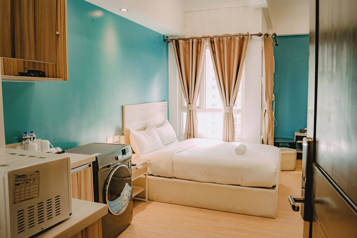 Quarto com cama, máquina de lavar, aquecedor e janela com cortinas.