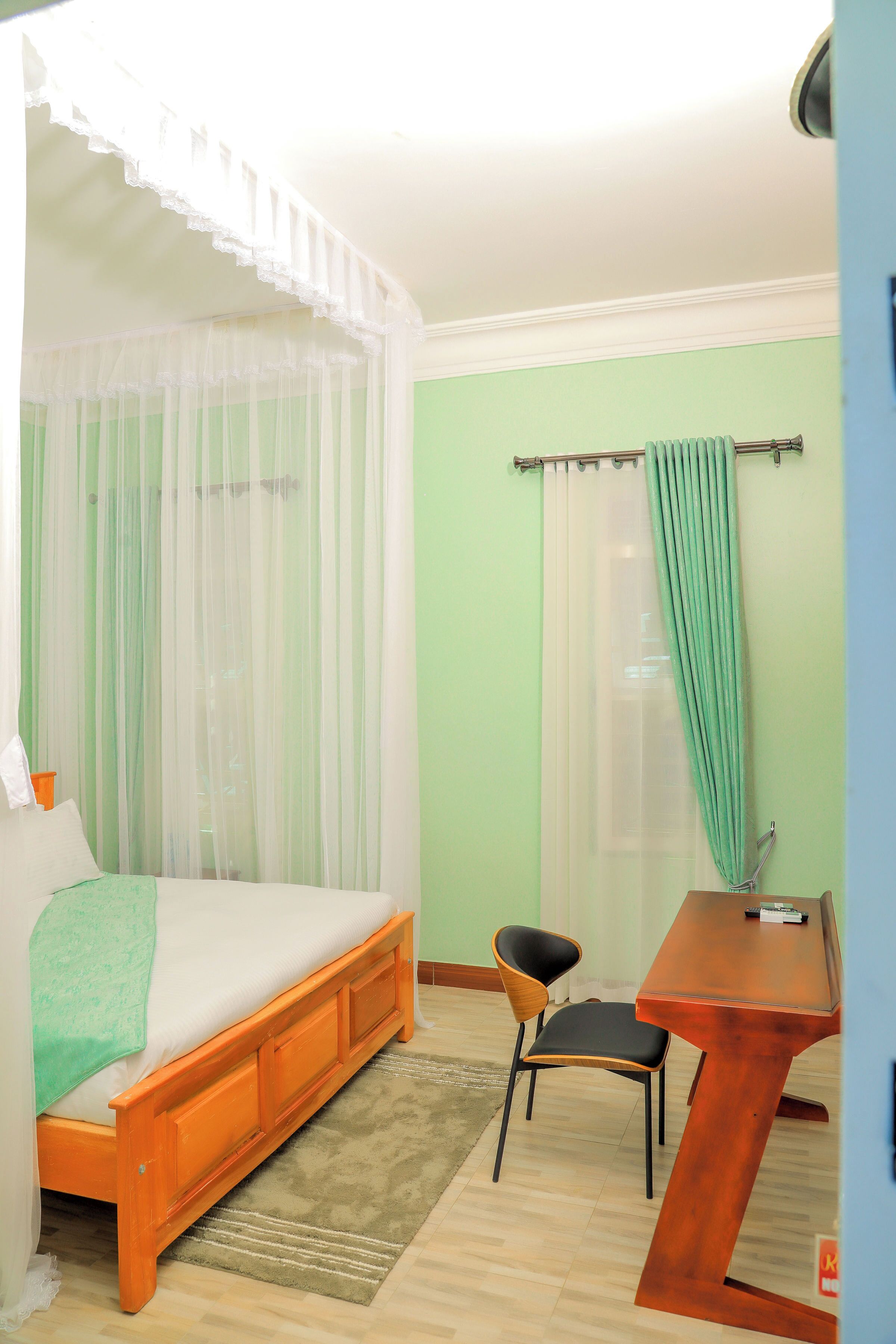 Um quarto com uma cama, uma cadeira, uma escrivaninha e uma janela com cortinas.