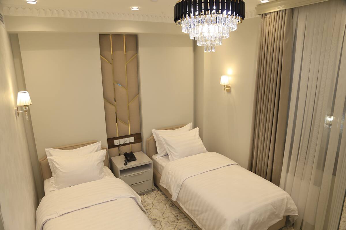 Quarto de hotel com duas camas, mesa de cabeceira com telefone, lustre e luminária na parede.