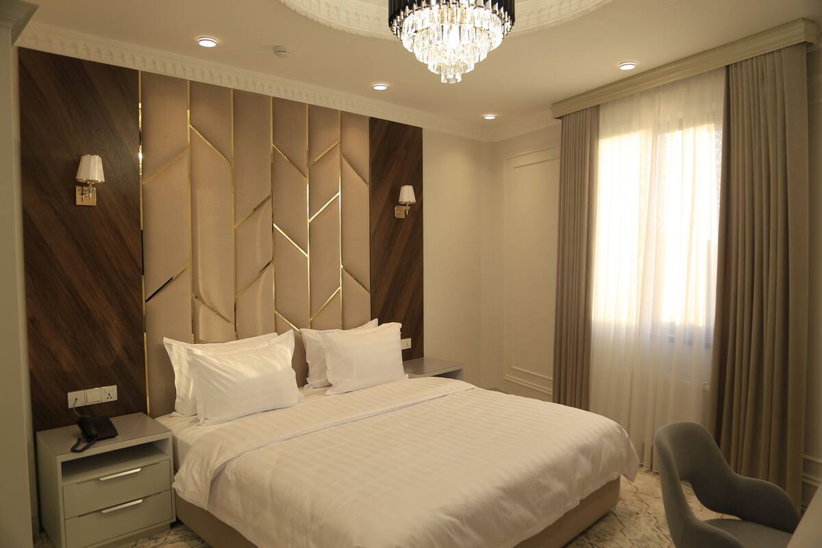 Quarto de hotel moderno com uma cama grande, uma mesa de cabeceira, uma cadeira e um candelabro.