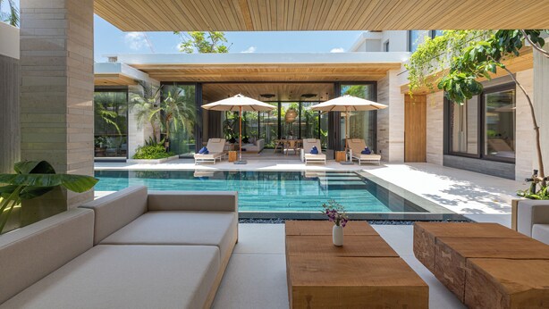 Uma área de piscina moderna com espreguiçadeiras, uma mesa de madeira e vista para a piscina.