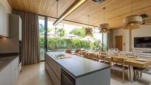 Cozinha moderna com uma ilha grande, área de refeições com mobiliário de madeira e vista para um jardim.