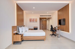 Quarto de hotel moderno com cama, mesa de cabeceira, escrivaninha, cadeira e TV fixada na parede.