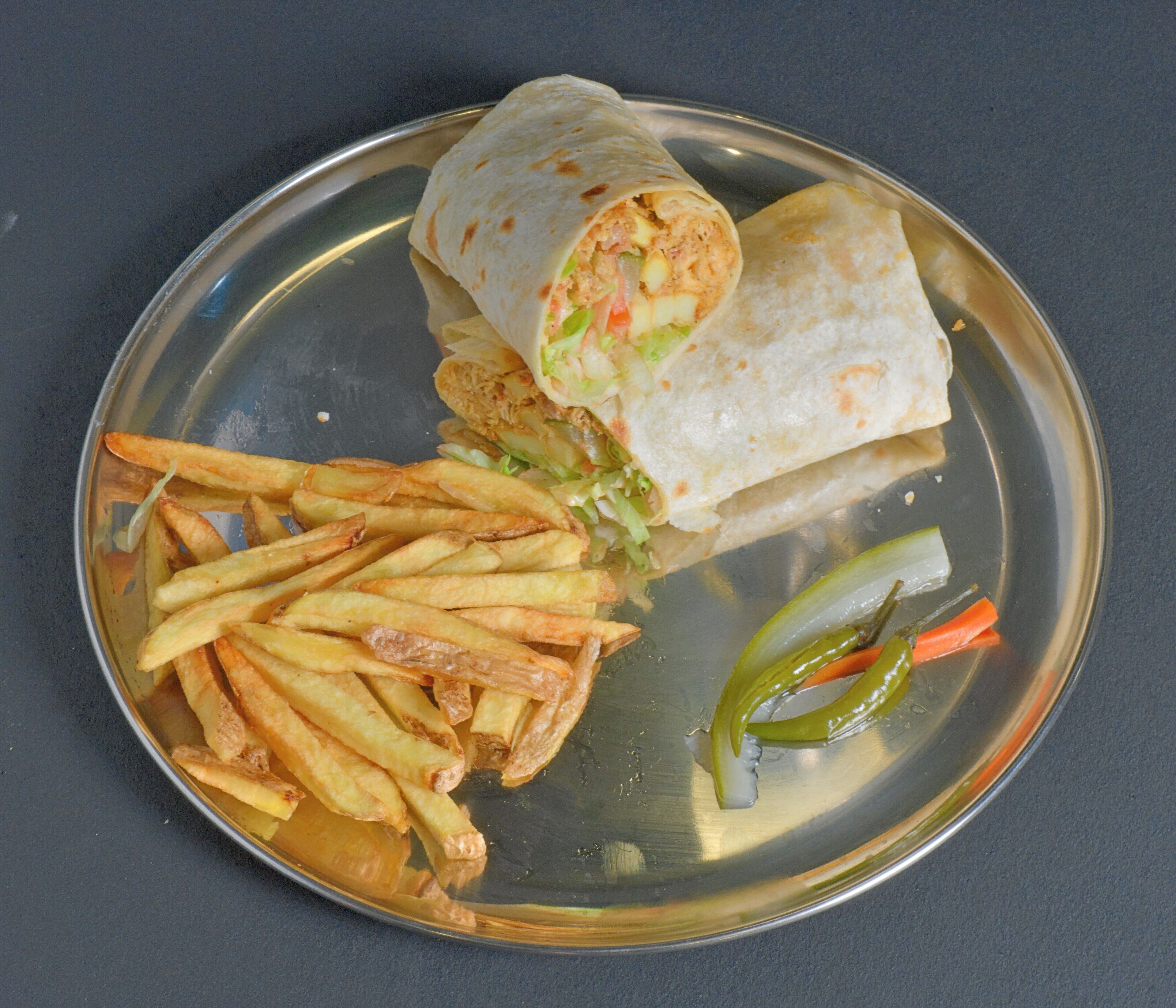 Um prato com um wrap, batatas fritas e legumes em conserva.