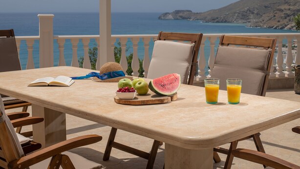 Mesa posta com livro, frutas e bebidas, com vista para a costa.