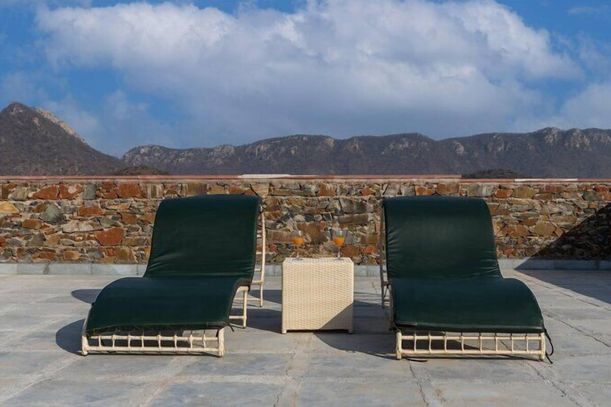 Duas poltronas de descanso com um muro de pedra e vista para as montanhas ao fundo.
