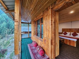 Uma cabana de madeira com uma cama, um banco com almofadas e vista para a floresta.