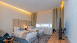 Quarto de hotel com duas camas, uma mesa, uma TV e uma mesinha.