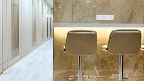 Um corredor com parede de mármore e dois bancos altos com pernas de metal.
