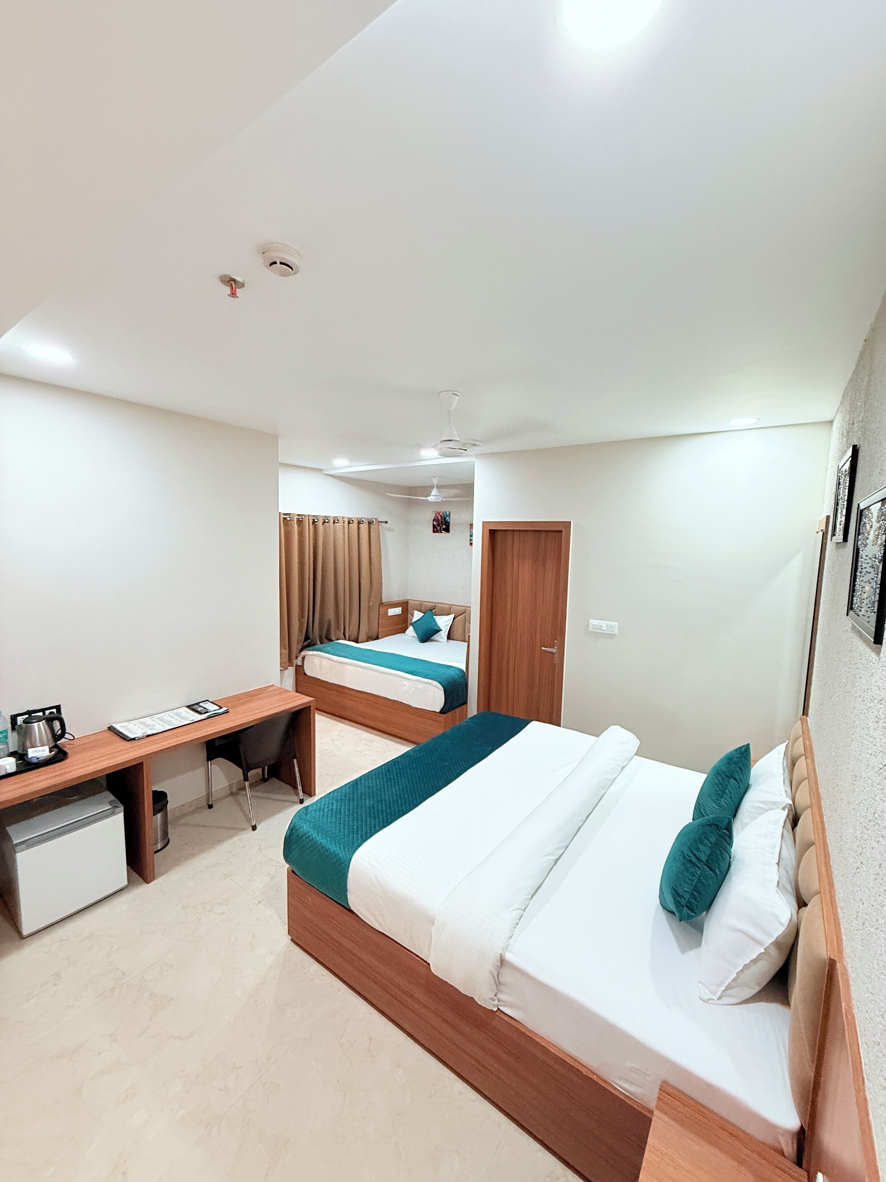 Quarto de hotel com duas camas, uma escrivaninha, uma cadeira, uma máquina de café e um pequeno frigorífico.