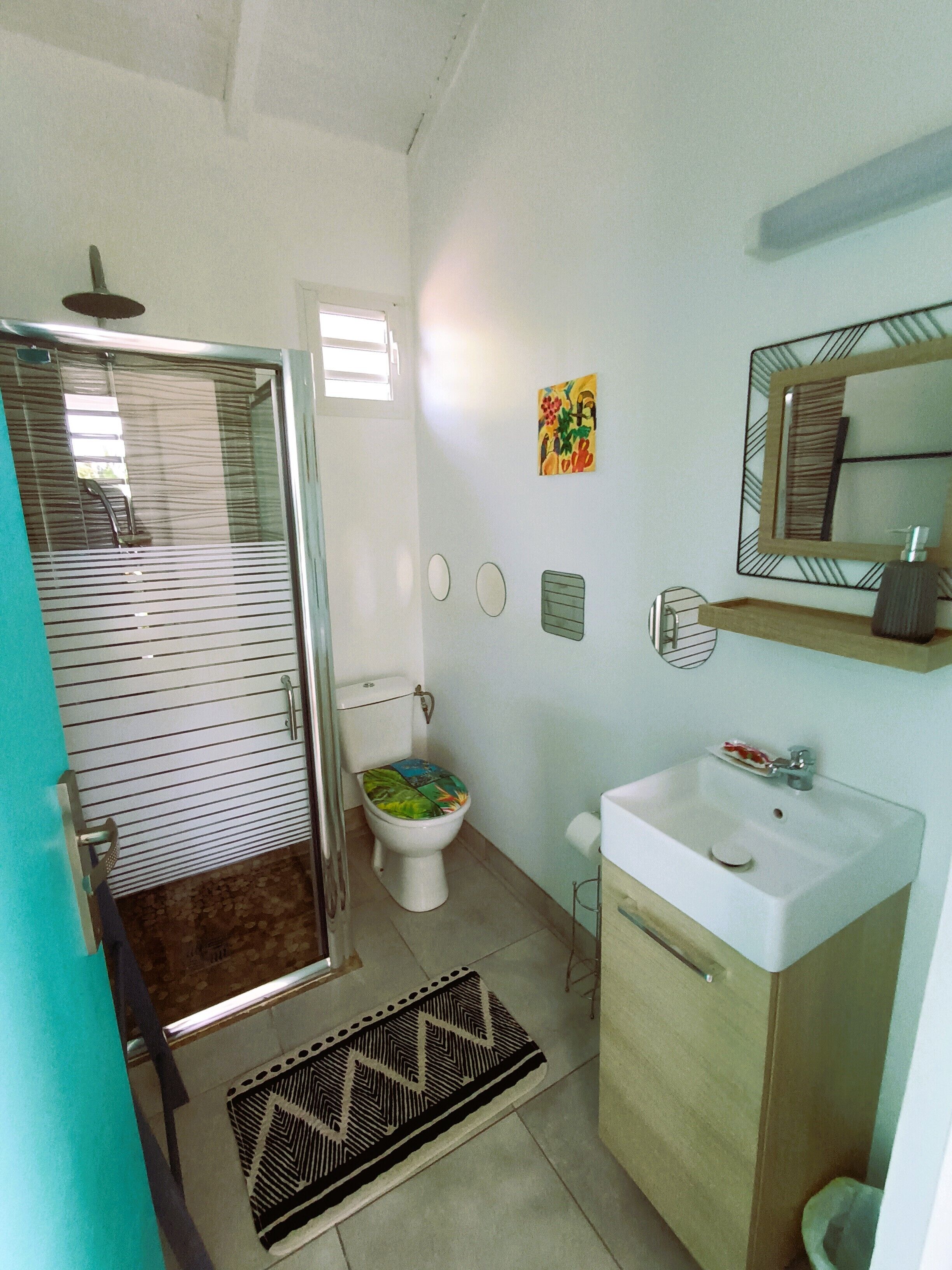 Casa de banho com sanita, lavatório, chuveiro e espelho decorativo.