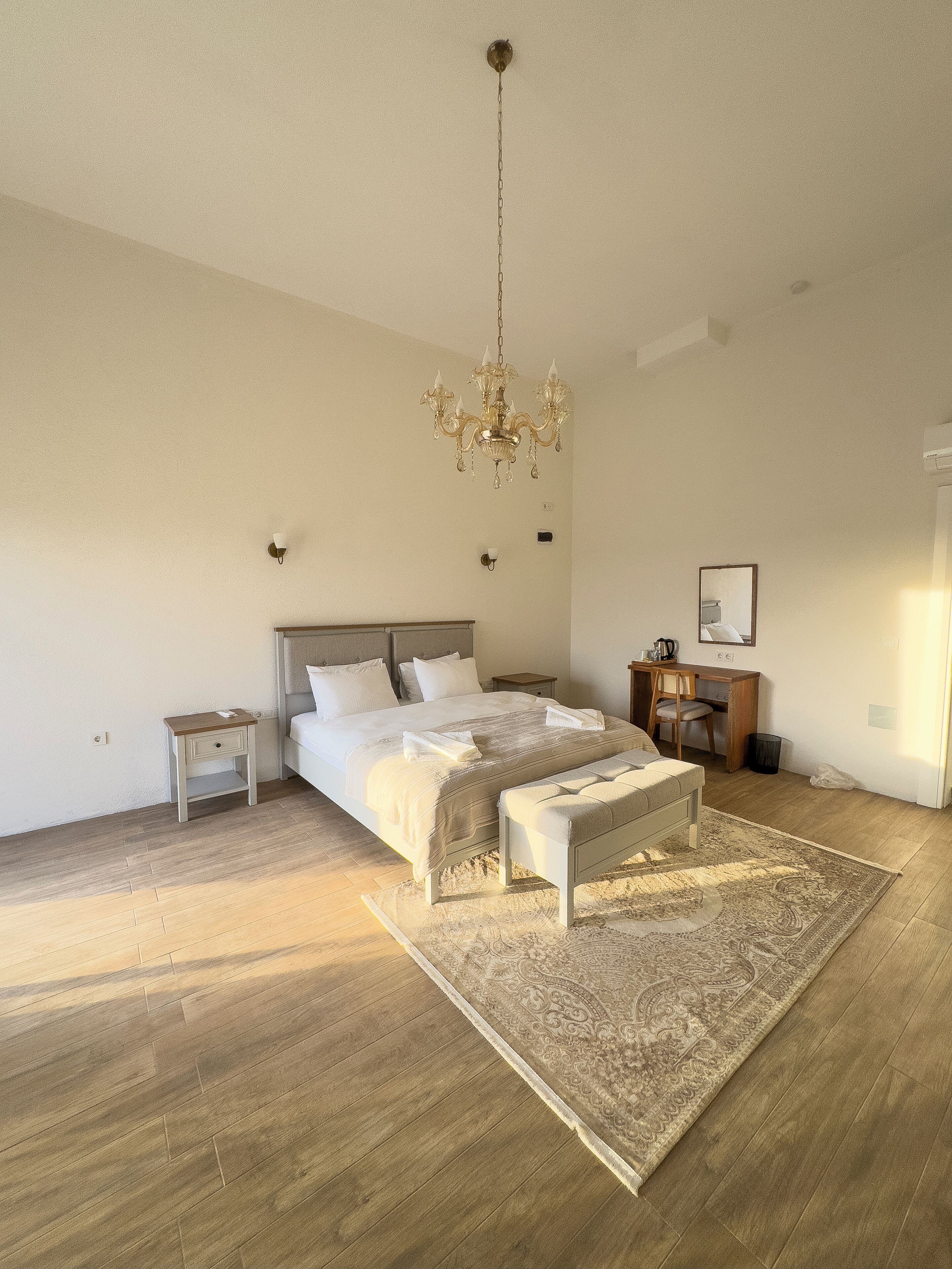 Quarto espaçoso com uma cama grande, mesa de cabeceira, escrivaninha e um candelabro.