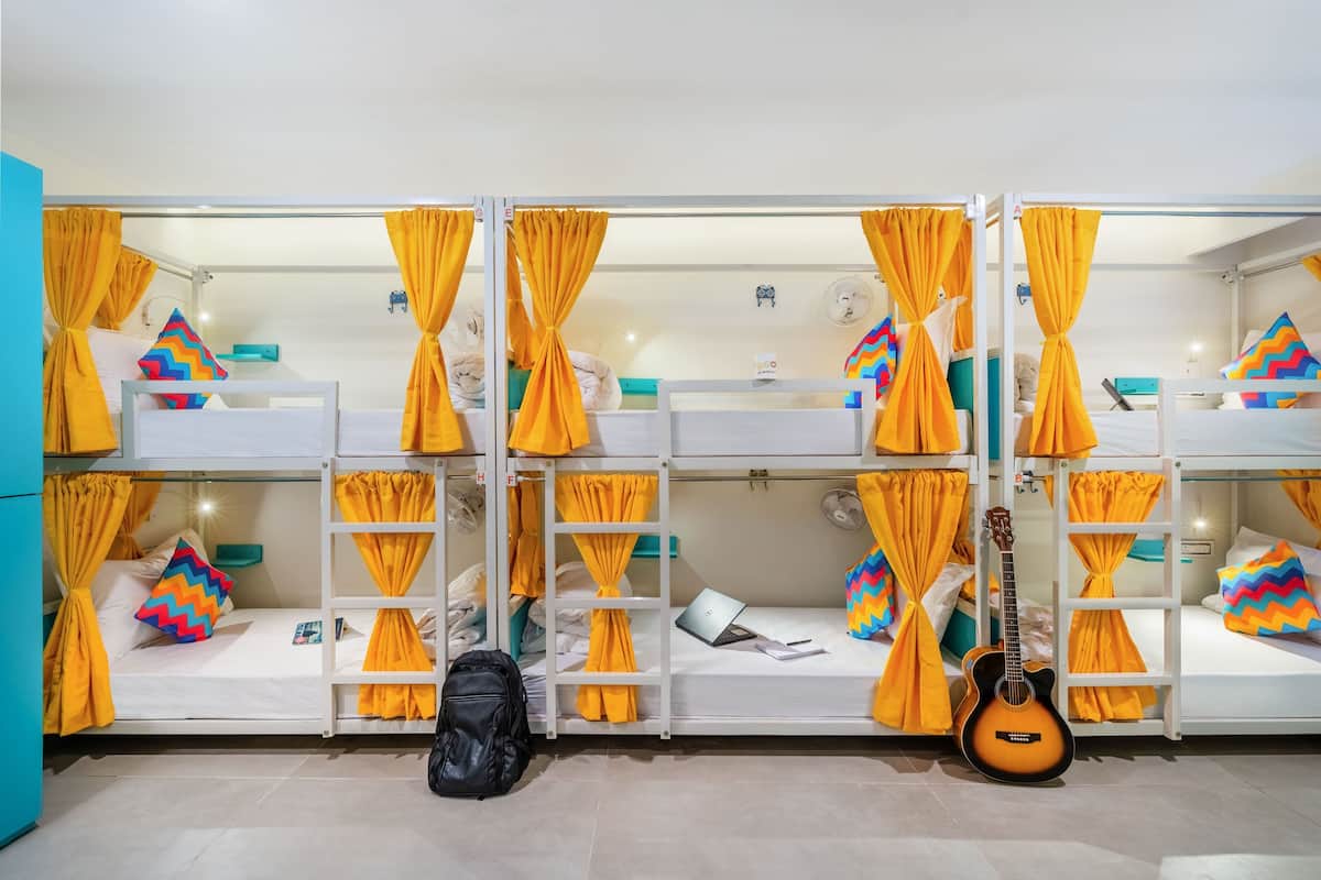 Um dormitório com beliches, cortinas amarelas, um violão e uma mochila.