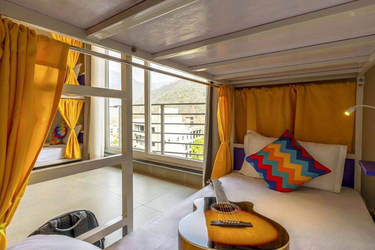 Quarto de hotel com cama, uma guitarra e janela com cortinas.