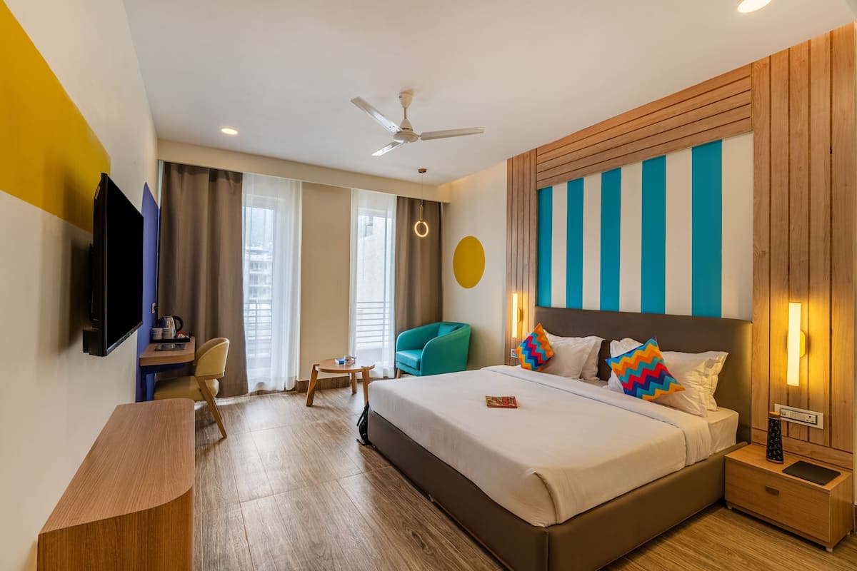 Quarto de hotel com uma cama grande, uma escrivaninha, uma cadeira, uma televisão e um ventilador de teto.