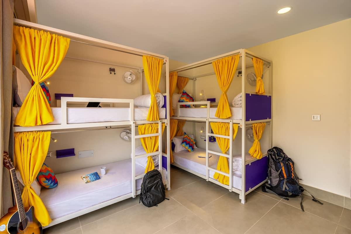 Um dormitório com beliches, cada um com cortinas amarelas, uma guitarra e uma mochila.