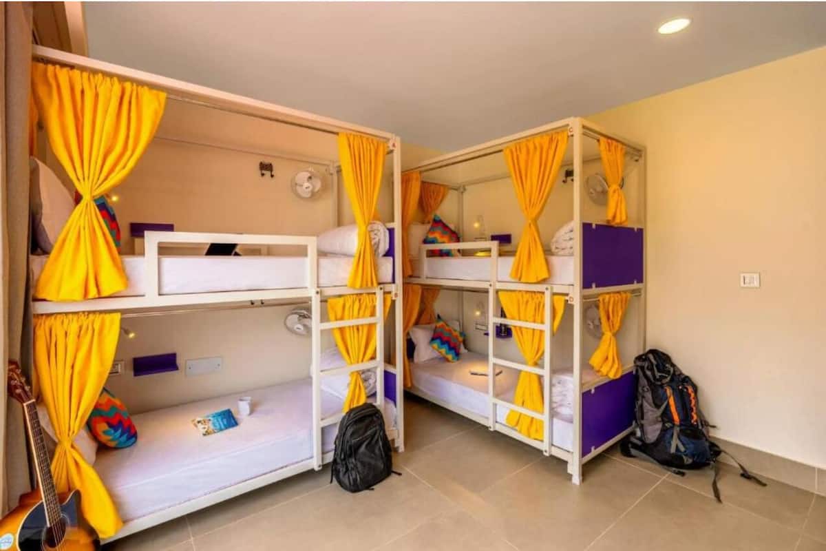 Um dormitório com beliches, cada um com cortinas amarelas, uma guitarra e uma mochila.