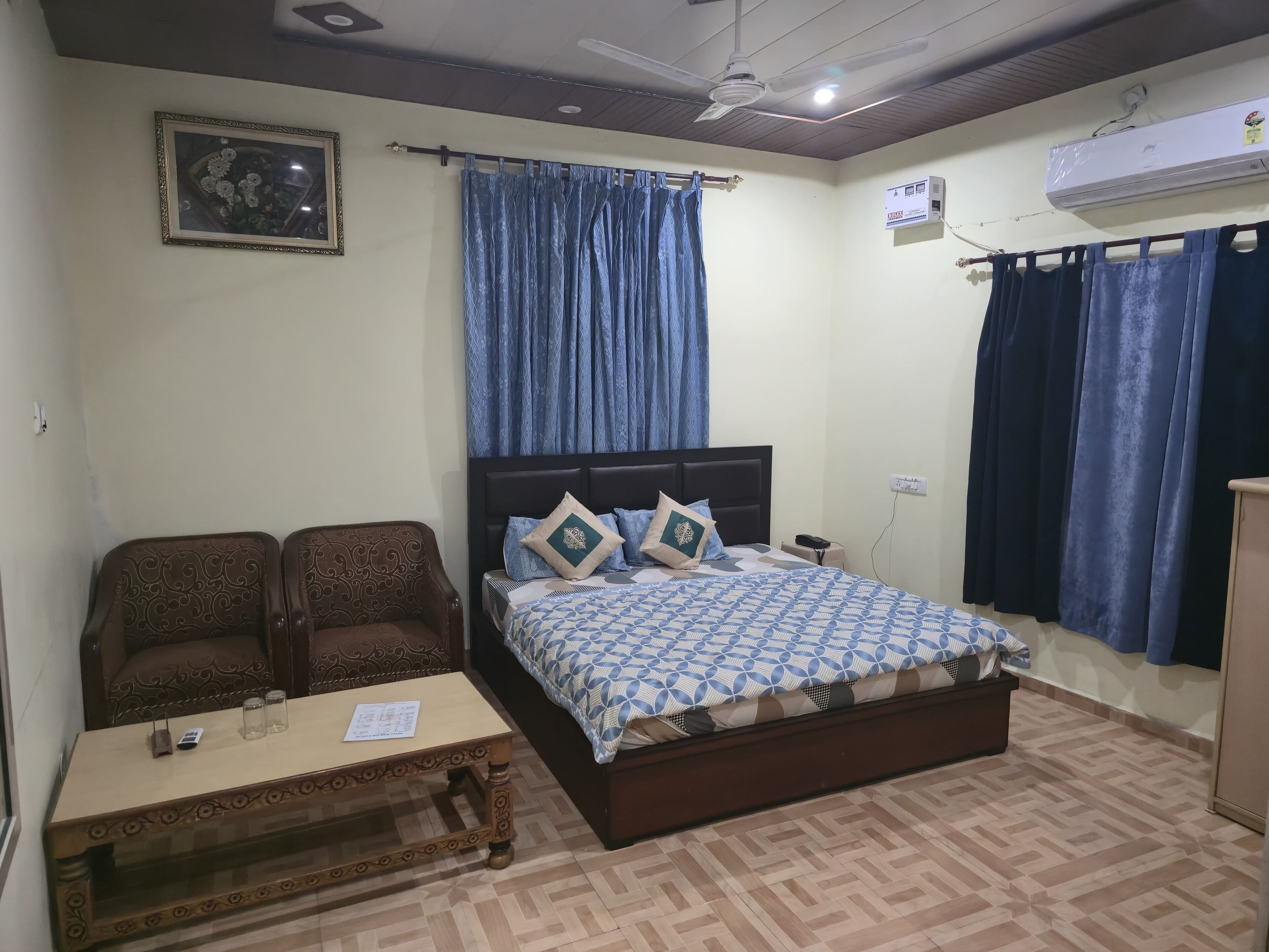 Quarto com cama, duas cadeiras, uma mesa pequena, ventilador de teto e ar condicionado.