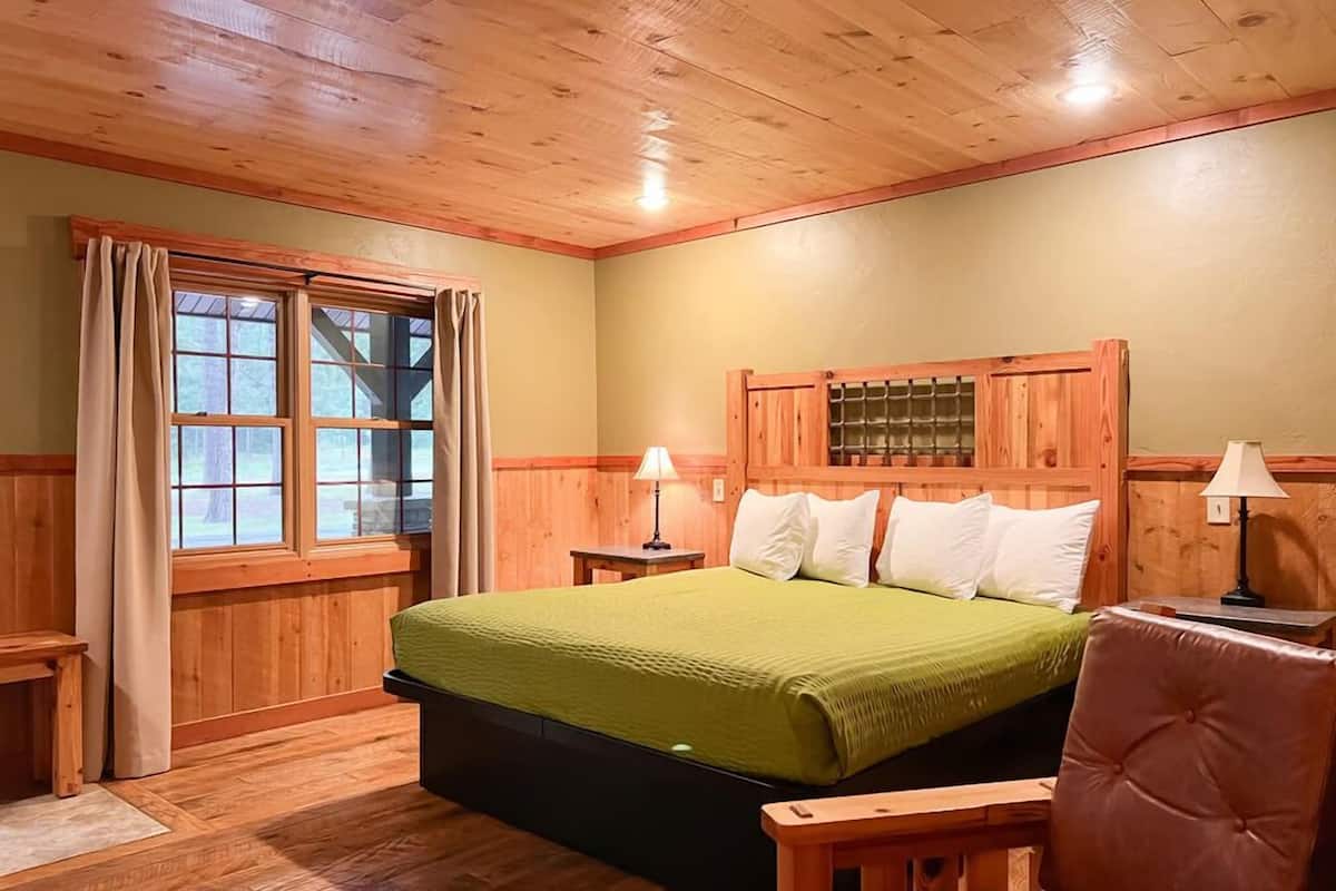 Quarto com painéis de madeira, uma cama, duas mesas de cabeceira e uma cadeira.