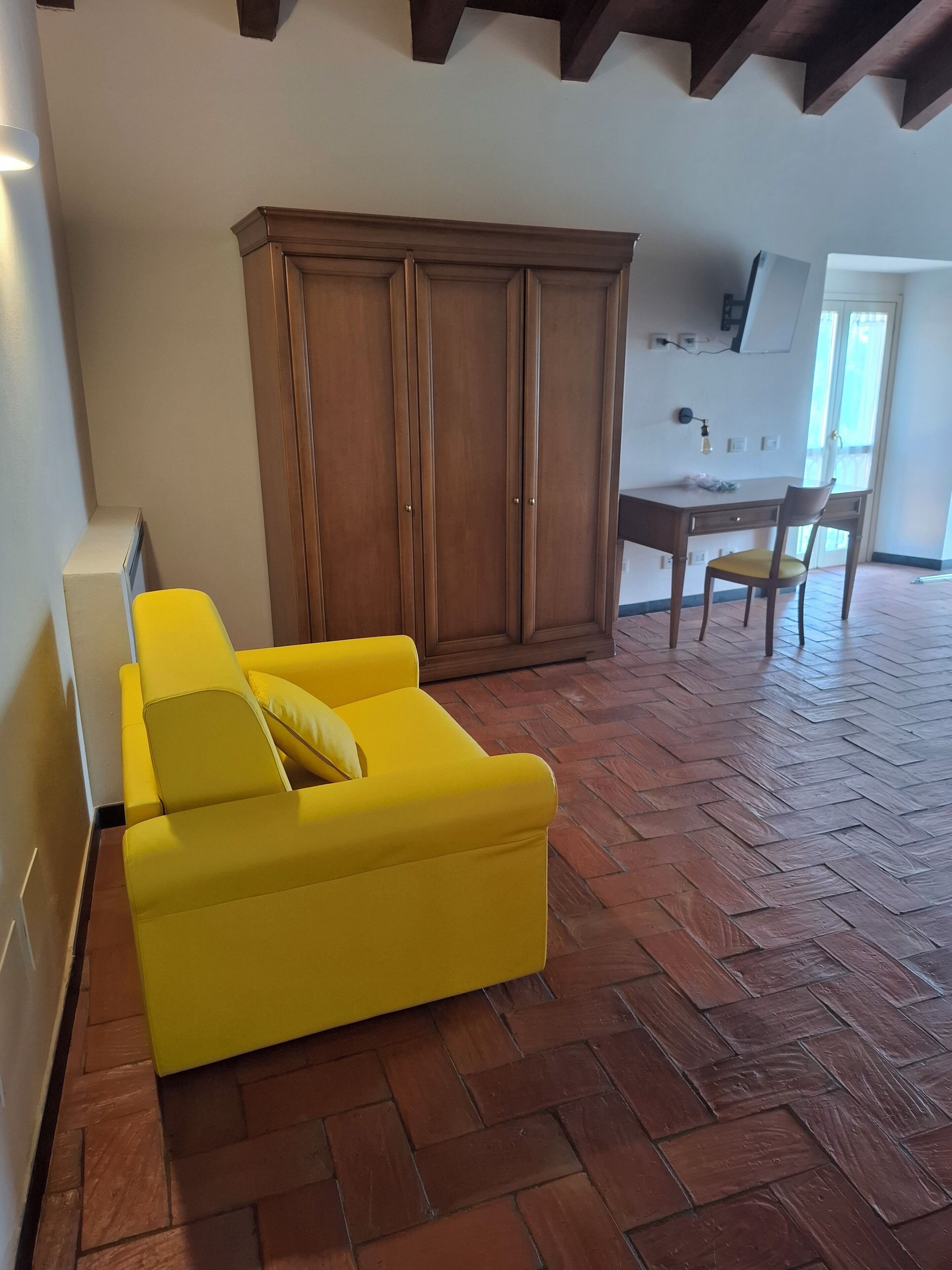 Quarto com sofá amarelo, guarda-roupa de madeira, mesa de jantar com cadeiras e chão ladrilhado.