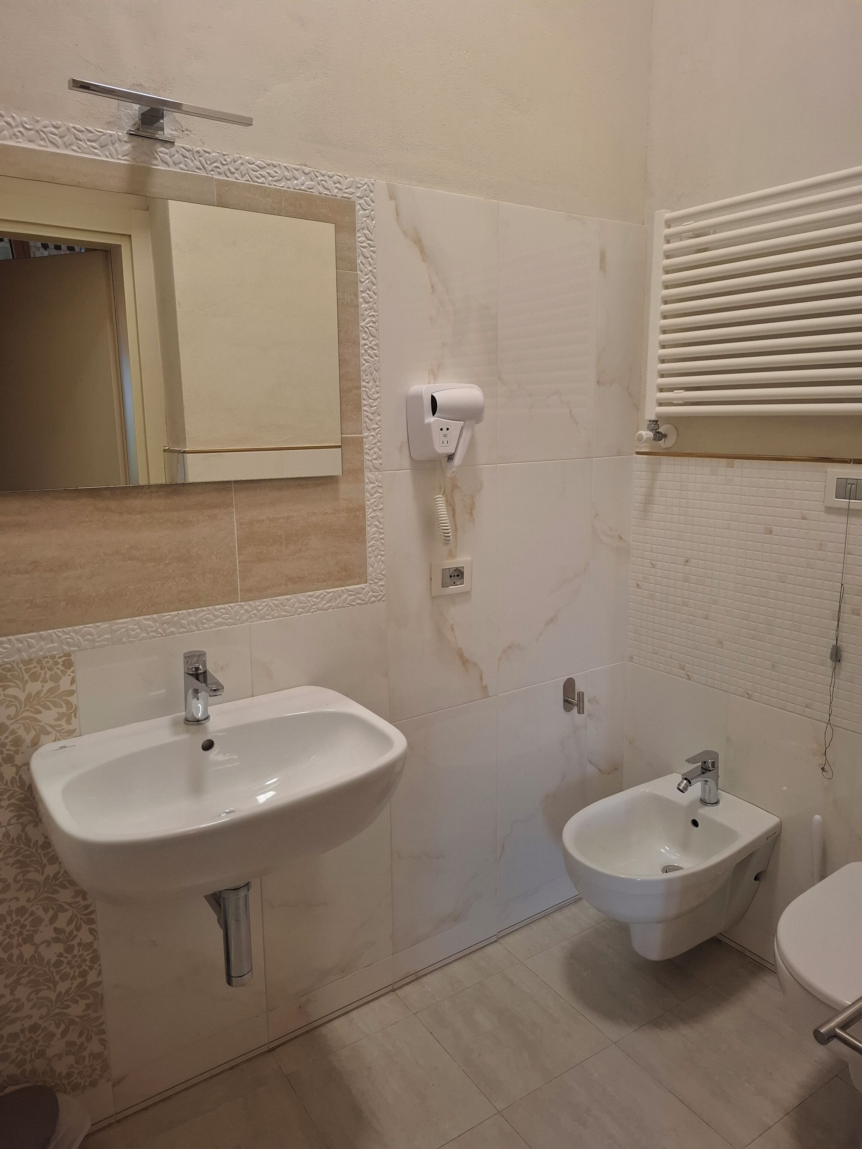 Casa de banho com duas pias, um bidé, uma sanita e um espelho, além de um porta-toalhas.
