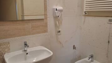 Casa de banho com duas pias, um bidé, uma sanita e um espelho, além de um porta-toalhas.