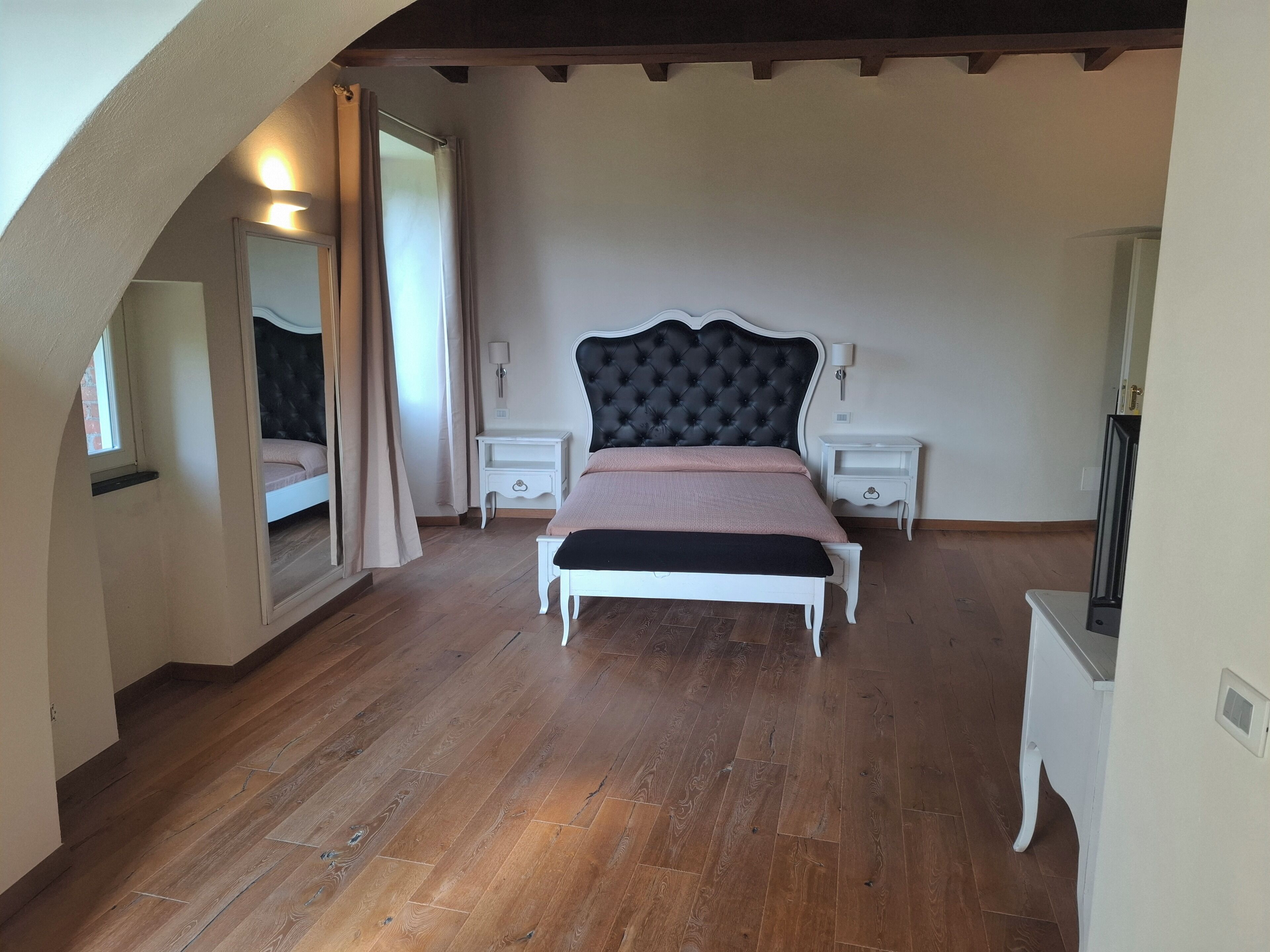 Quarto com uma cama grande, duas mesas de cabeceira, um espelho e piso de madeira.