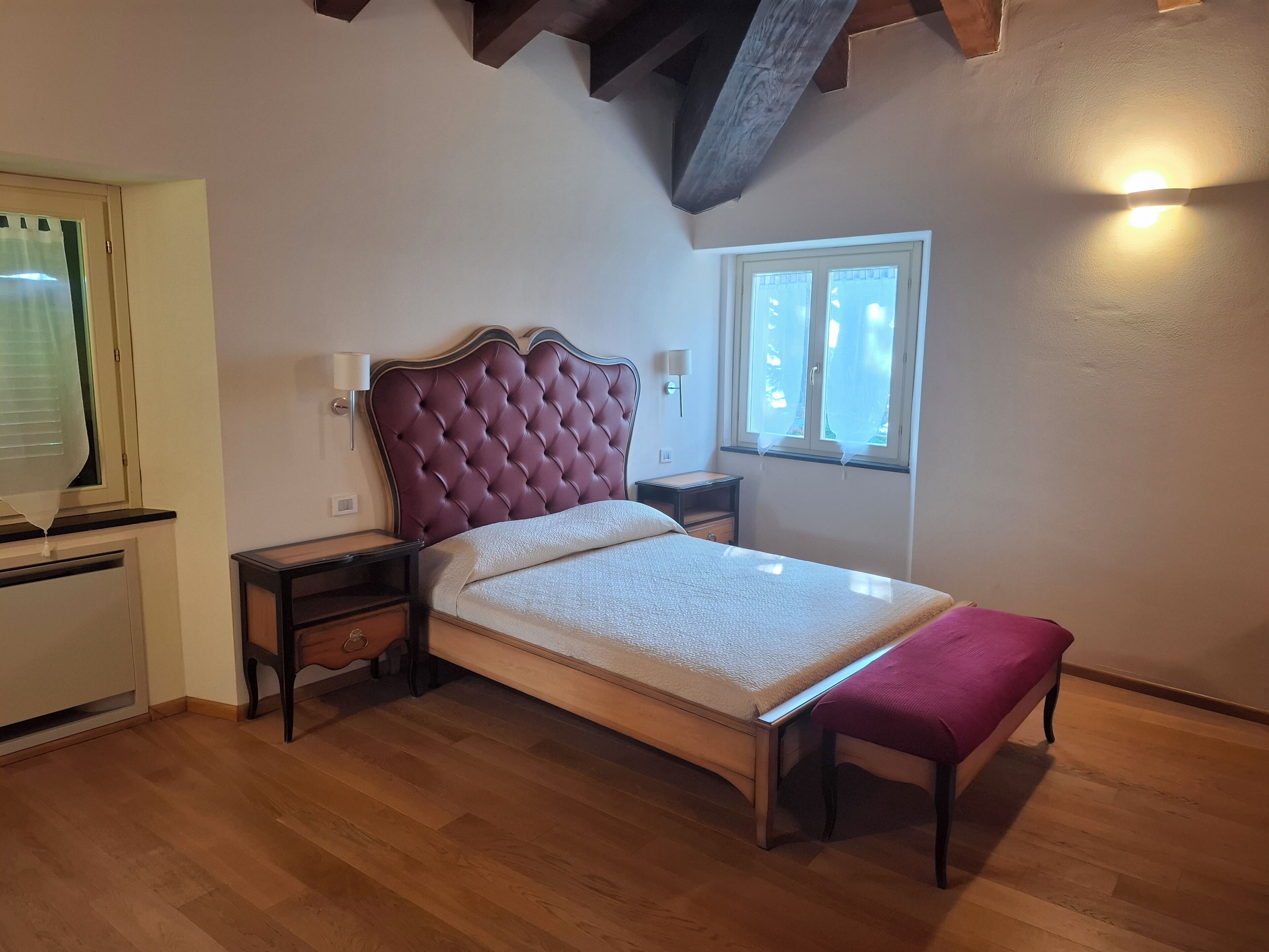 Quarto com cama, piso de madeira, janela e mesa de cabeceira.