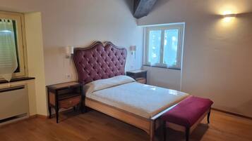 Quarto com cama, piso de madeira, janela e mesa de cabeceira.