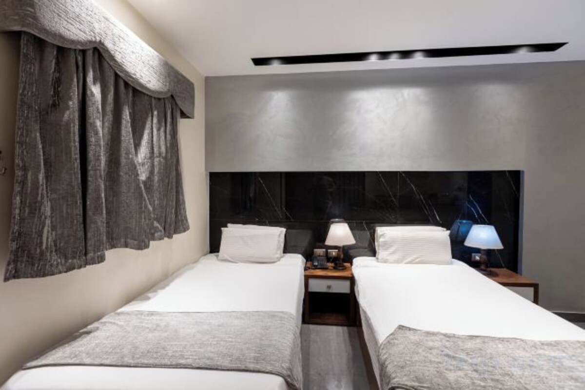 Quarto de hotel com duas camas, um espelho grande e uma mesa de cabeceira com abajur.