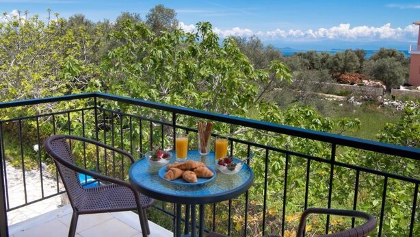 Varanda com mesa posta para o pequeno-almoço, incluindo croissants, fruta e sumo de laranja.