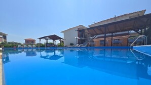 Piscina azul cristalina com espreguiçadeiras e um espaço de estar coberto.