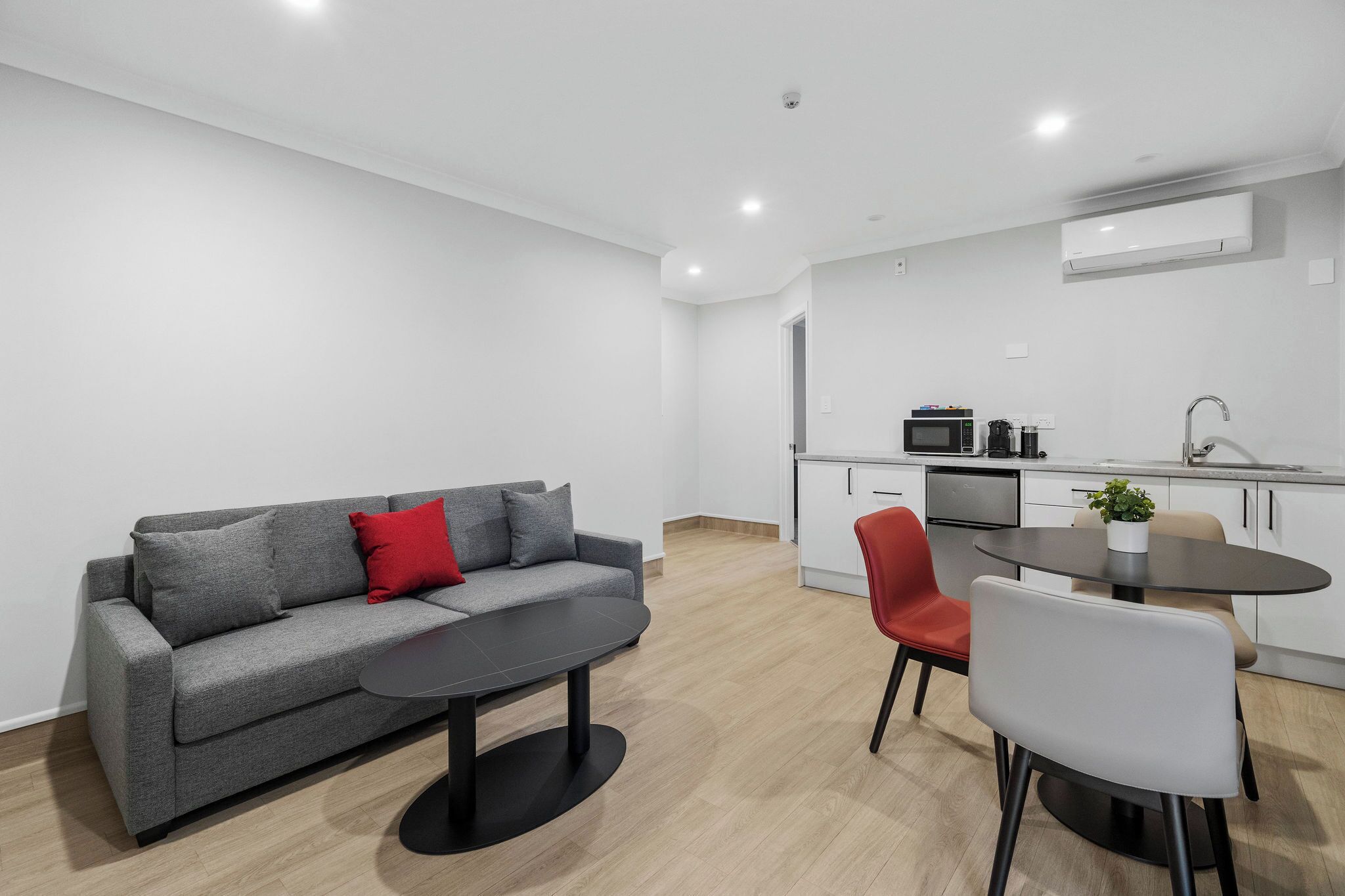 Uma sala de estar moderna com um sofá cinzento, uma mesa redonda e uma cadeira vermelha.