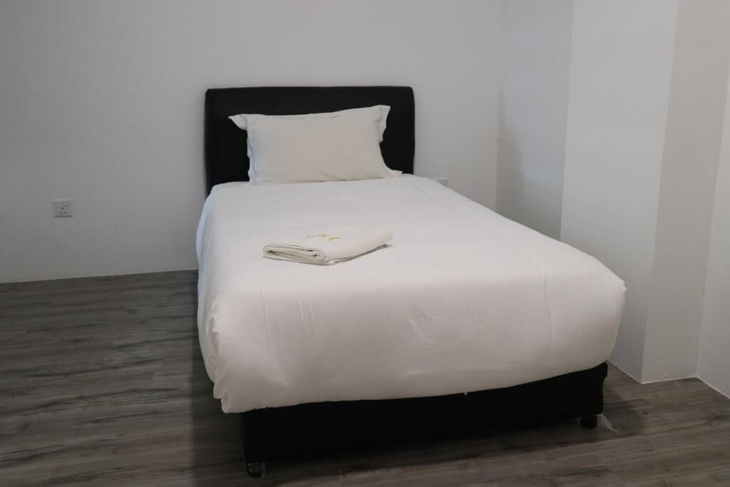 Uma cama de solteiro com colchão branco e cabeceira preta em quarto com piso de madeira e paredes brancas.