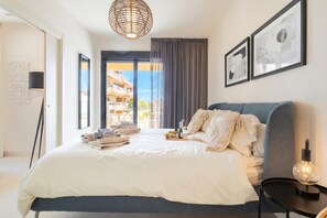 Quarto moderno com uma cama grande, mesa de cabeceira com luminária e vista para o exterior.