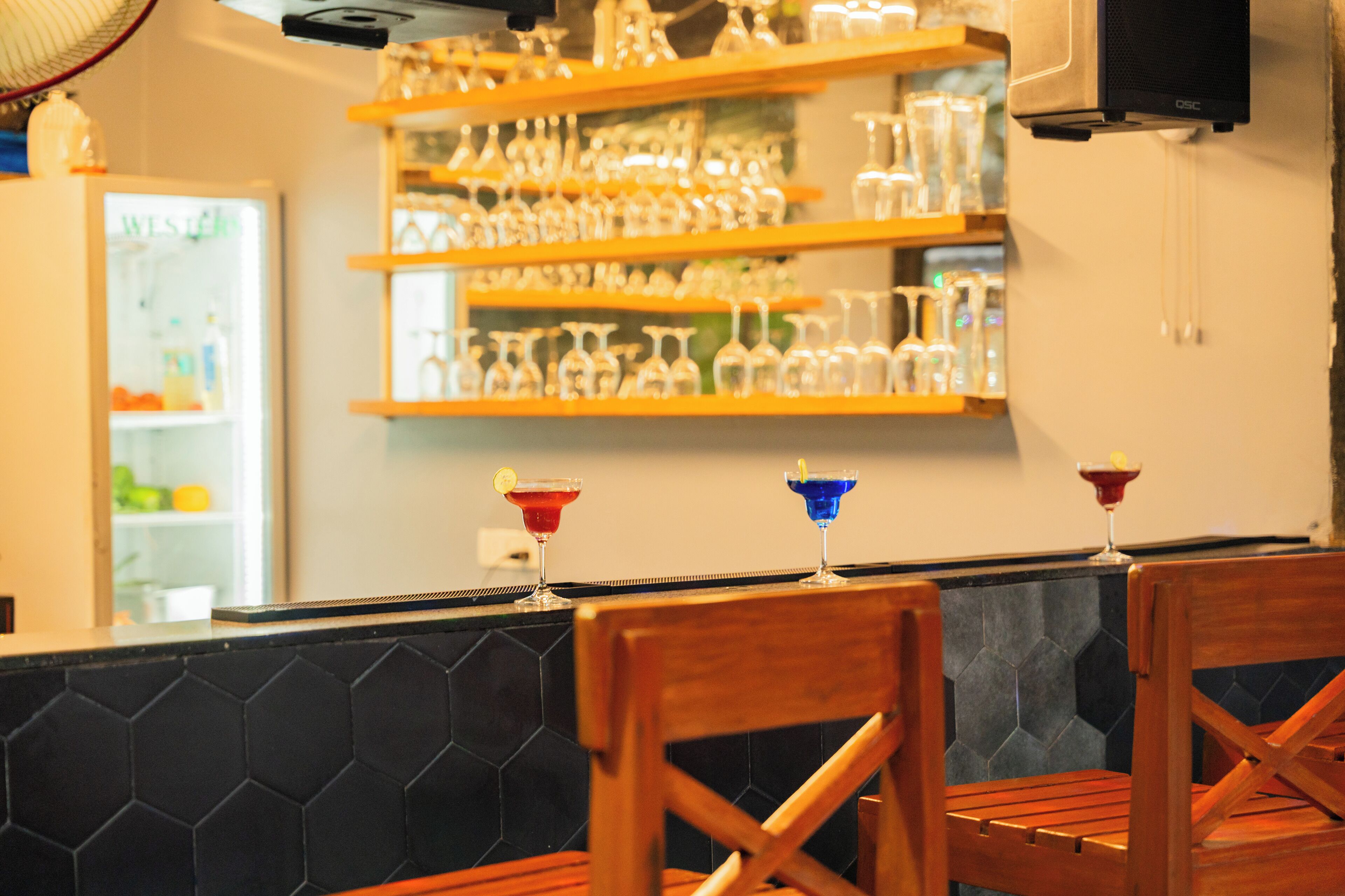 Uma área de bar com cadeiras de madeira e prateleiras cheias de copos e garrafas.