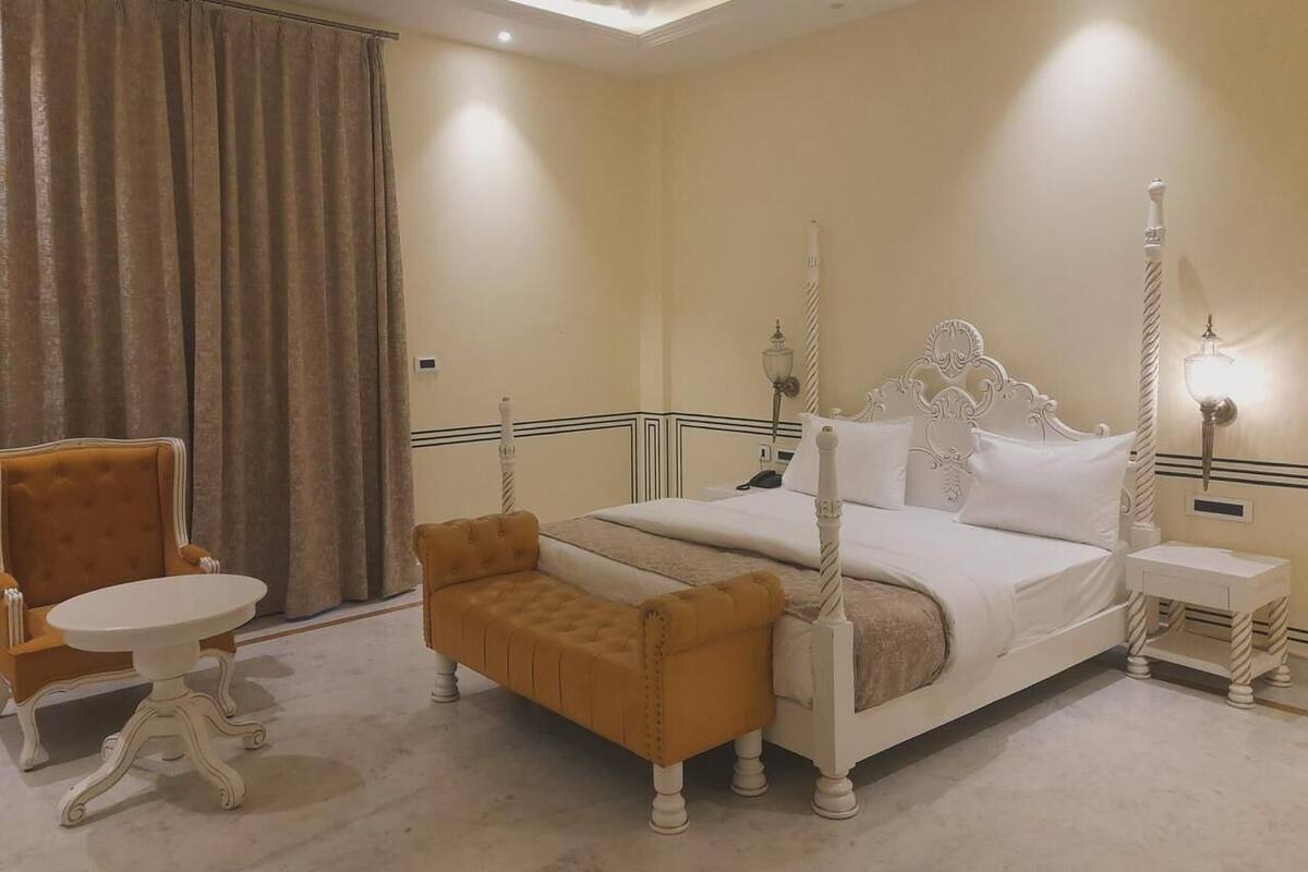 Quarto de hotel com cama de dossel, mesa redonda, um banco e uma mesinha de cabeceira.