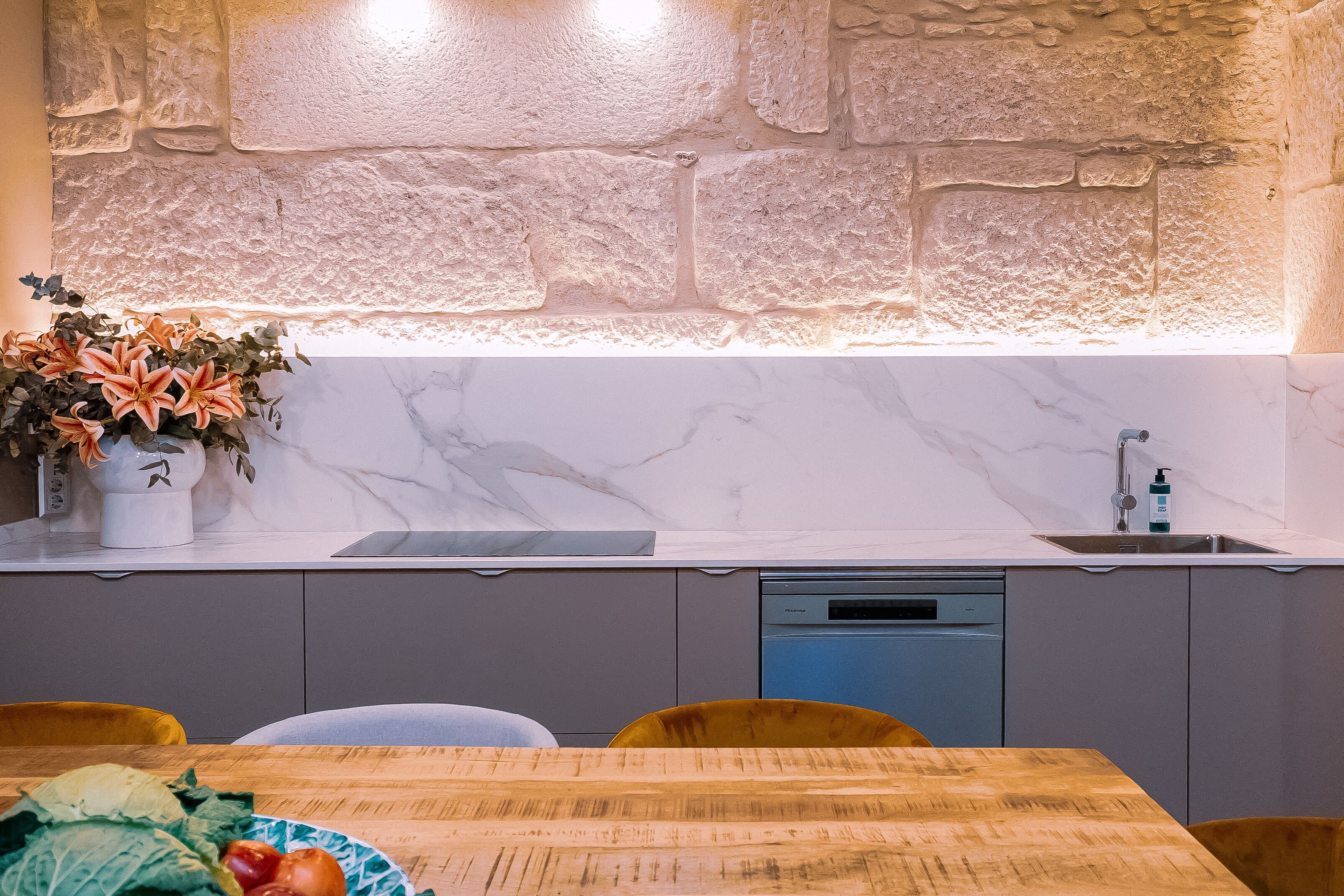 Cozinha moderna com bancada de mármore, máquina de lavar louça embutida e painel de parede revestido em pedra.