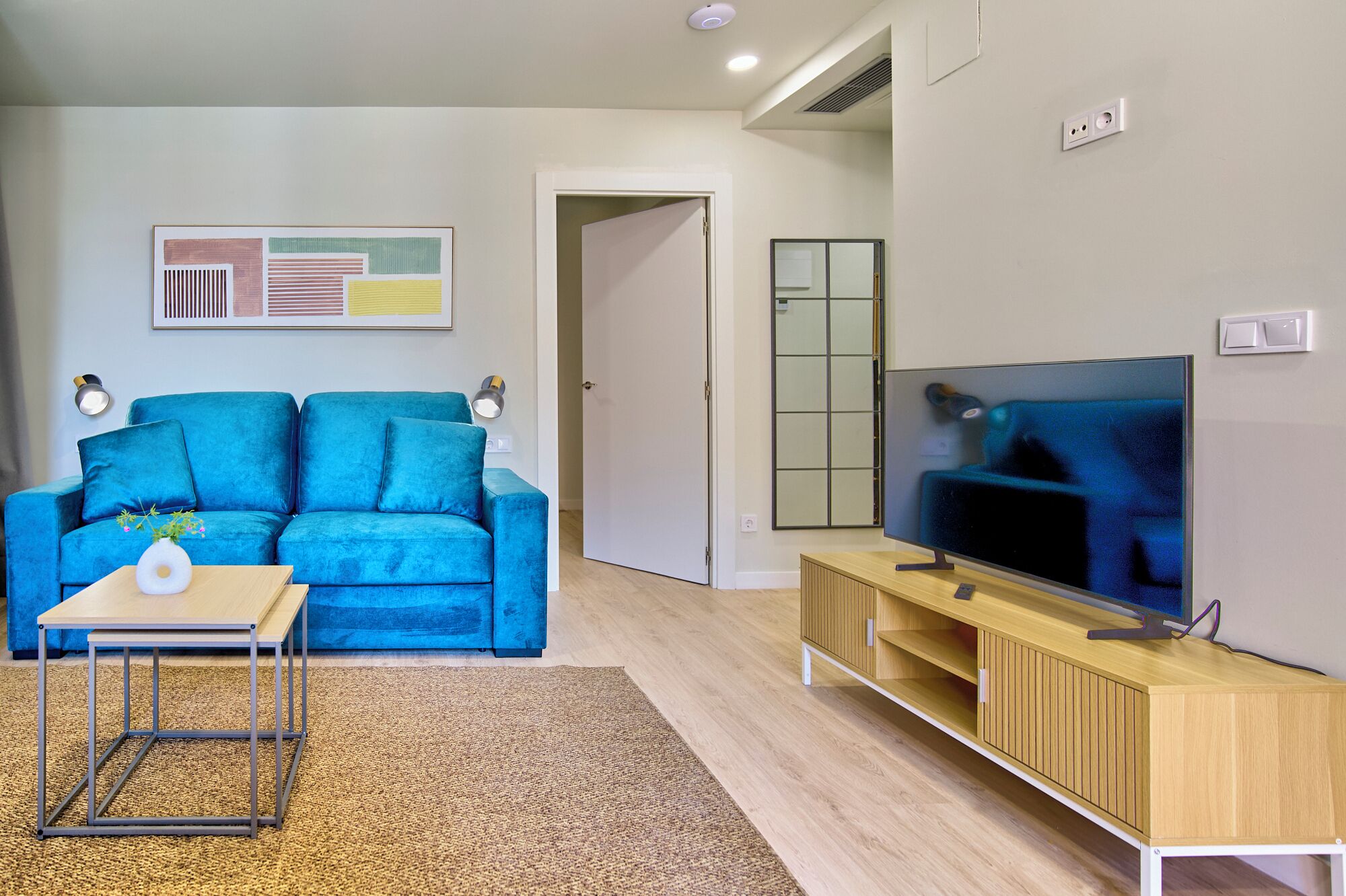 Uma sala de estar com um sofá azul, uma mesa de centro, uma TV em um suporte de madeira e um quadro na parede.
