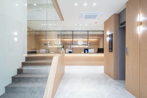 Uma área de recepção de hotel moderna com divisória de vidro, balcão de atendimento e escada para um andar superior.