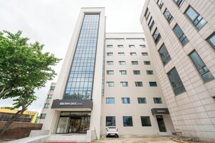Um hotel moderno com fachada de vidro destacada e uma placa com a inscrição "BROWN DOT HOTEL".