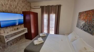 Quarto de hotel com cama, televisão, guarda-roupa, um quadro e janela com cortinas.