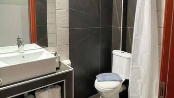 Um banheiro moderno com um espelho grande, uma pia branca, vaso sanitário e área de chuveiro.