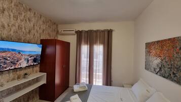 Quarto de hotel com cama, televisão, guarda-roupa, um quadro e janela com cortinas.